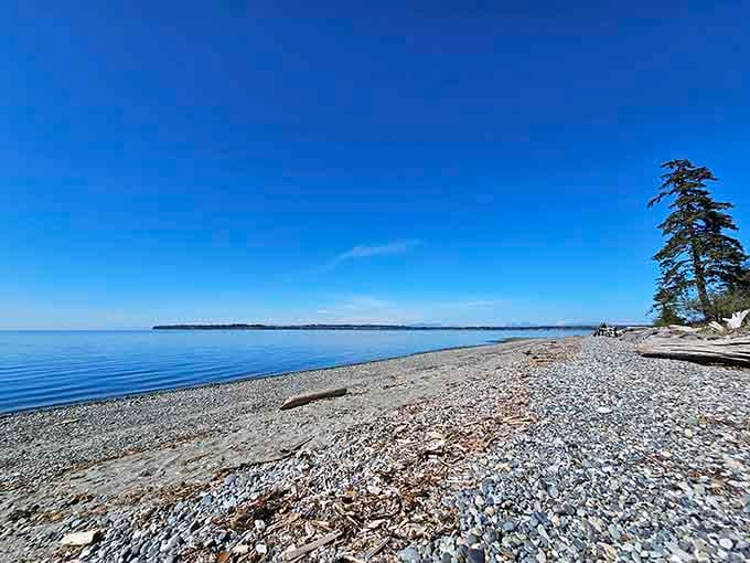 Smooth stones carpet the shoreline where crystal-clear water reflects the endless Pacific Northwest sky above.