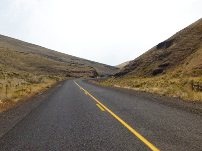 That yellow stripe leads straight to adventure, cutting through golden grasslands beneath moody skies that photographers dream about.
