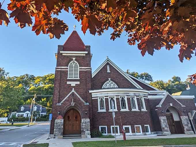 Autumn leaves frame this beautiful brick church like nature's own stained glass window against blue sky.