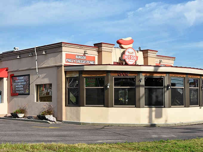 The cheerful mascot character waves from the rooftop, promising burgers and Philly cheesesteaks alongside those famous hot dogs.