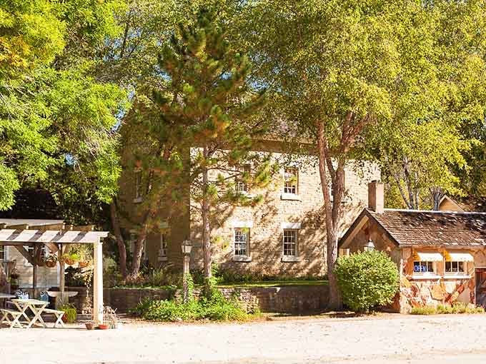 Sunlight filtering through ancient trees onto historic stone buildings creates a scene straight from a storybook illustration.