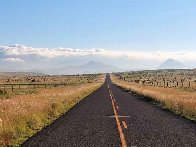Twin peaks rise like natural monuments while the asphalt ribbon winds through a landscape dotted with hardy desert vegetation.