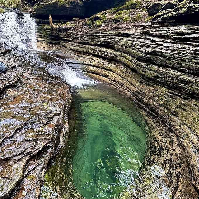 Cascading waterfall plunges into crystal-clear pool surrounded by moss-covered stone walls and lush greenery.