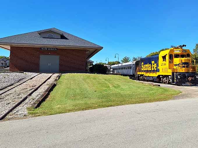 The restored brick depot and sunny yellow locomotive create a postcard-worthy scene of small-town railroad heritage.