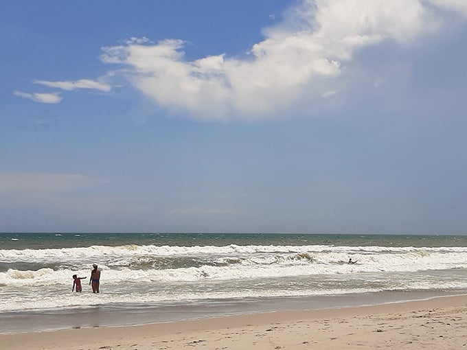 Two beachgoers enjoy the gentle waves at this peaceful stretch of coastline under wide open skies.