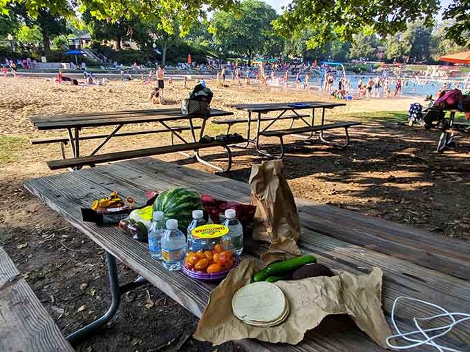 Fresh fruit and sandwiches spread on weathered picnic tables, because swimming works up an appetite that demands immediate satisfaction poolside.