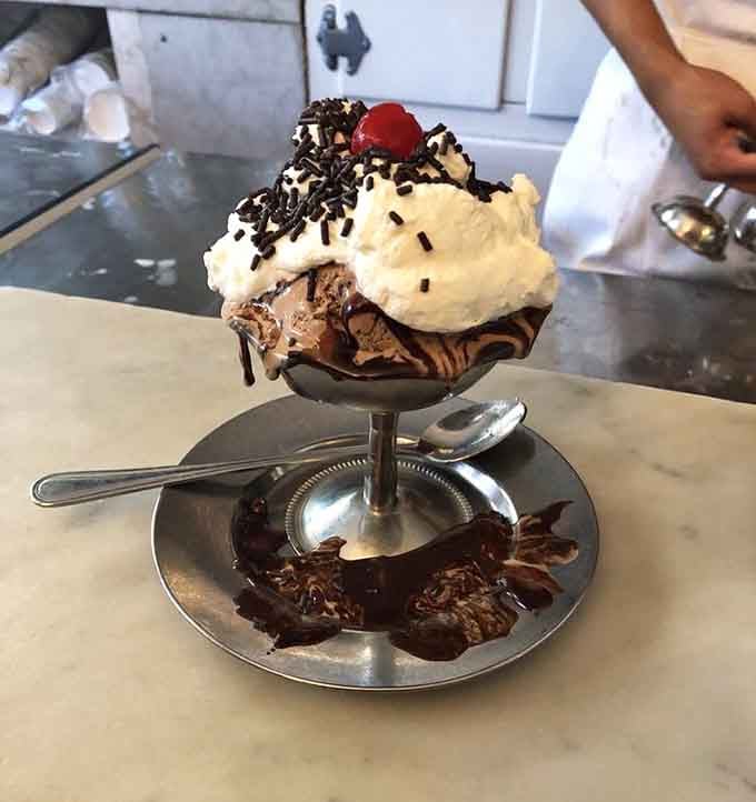 Chocolate sauce cascades like a delicious waterfall over ice cream peaks that defy both gravity and restraint.