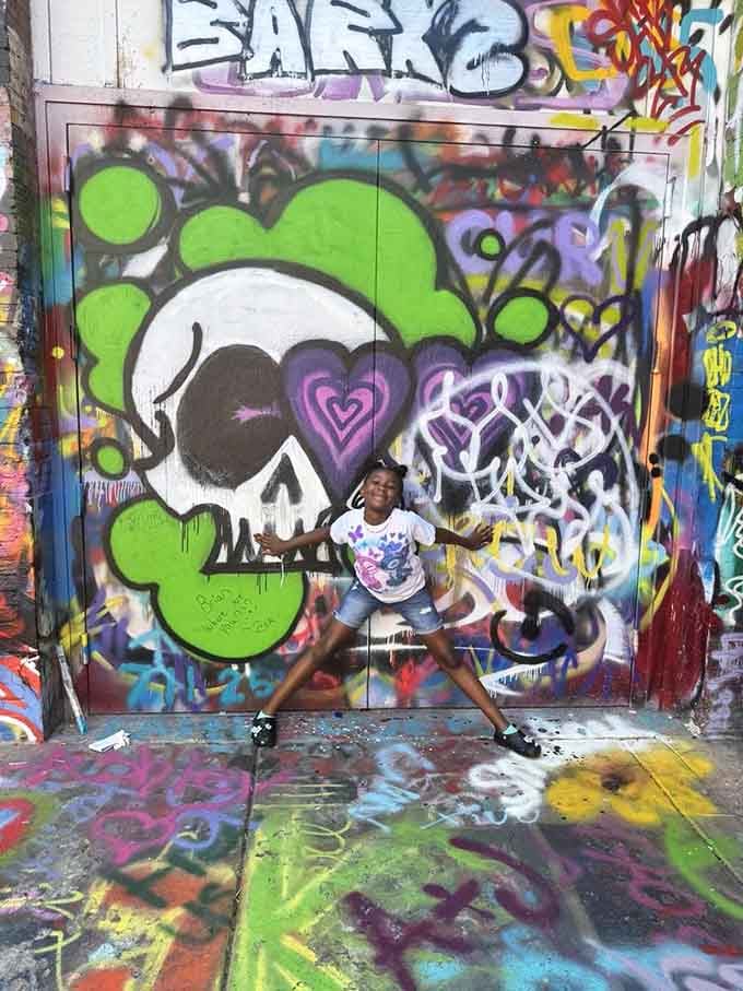 Pure joy captured in front of a skull mural—proof that street art brings out the kid in all of us.