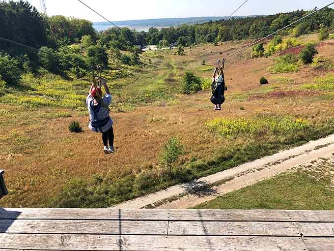 Two adventurers race side by side across open terrain, turning a simple zipline into friendly competition.