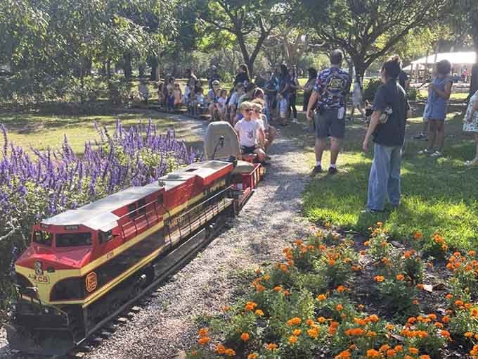 Sunshine filters through oak canopy as the locomotive chugs past blooming flowers, creating a scene Norman Rockwell would've painted.