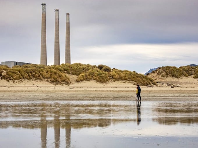 Those vintage power plant stacks create an unexpectedly dramatic backdrop, like industrial art meeting endless shoreline.
