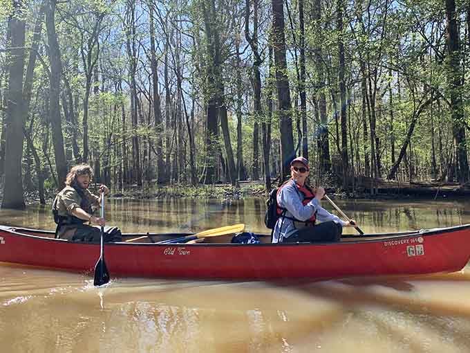Tandem canoeing through waters that look like sweet tea, proving teamwork makes the dream work on any river.