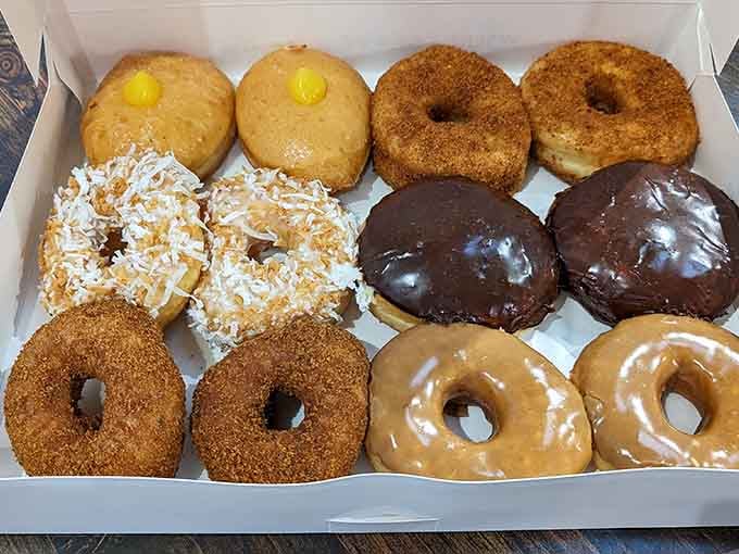 A dozen donuts arranged like edible art, from coconut-covered to chocolate-glazed perfection in one beautiful box.