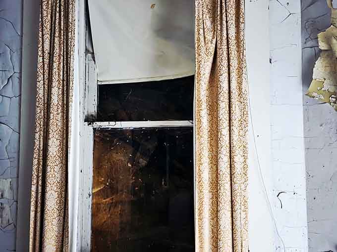 Those tattered curtains hanging in broken windows look like they're auditioning for a haunted house movie set piece.