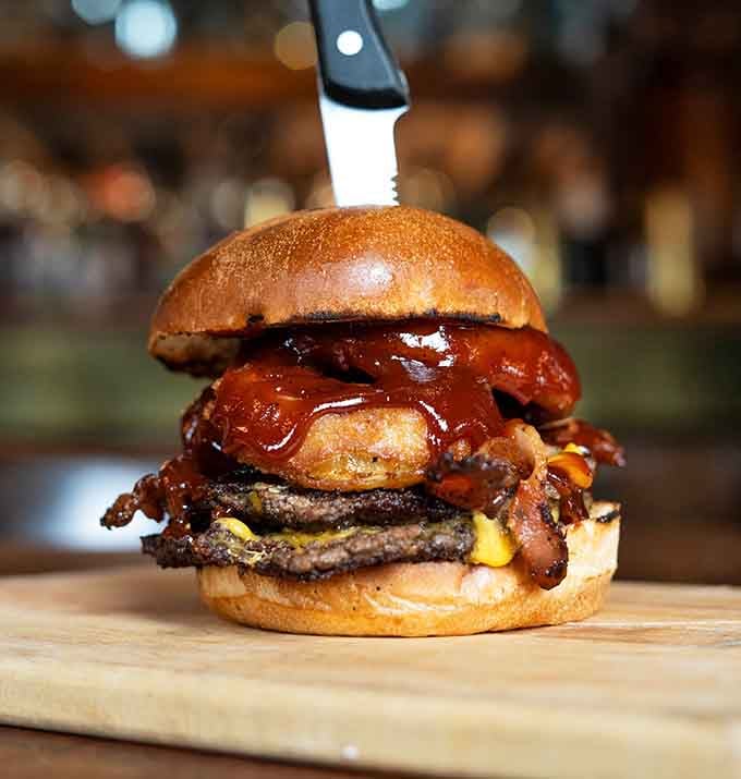 This towering burger stacked with bacon and onion rings makes architectural engineering look absolutely delicious and completely necessary.