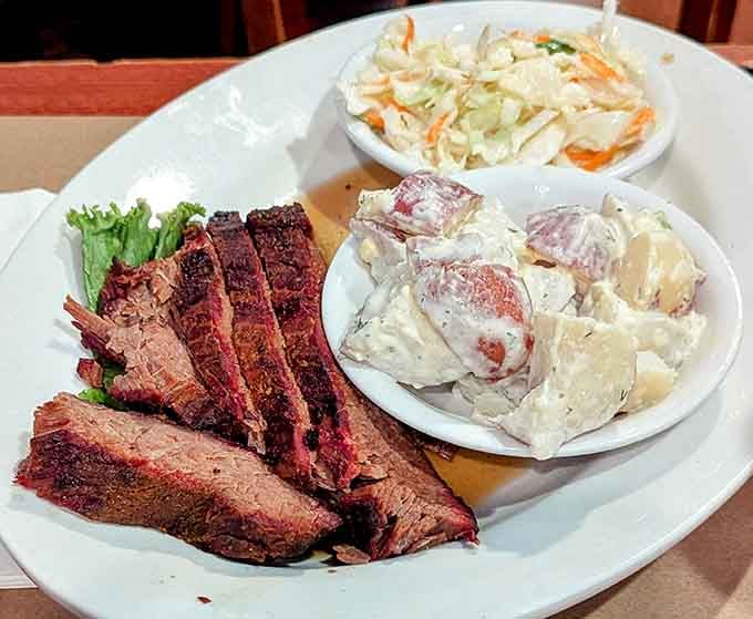 Sliced brisket with that perfect smoke ring, flanked by creamy potato salad and fresh coleslaw perfection.
