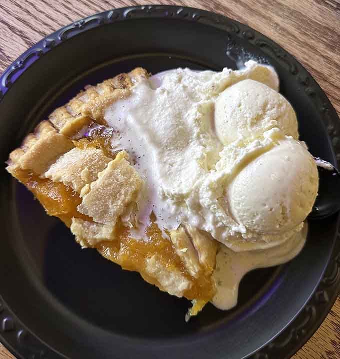 Warm peach pie topped with vanilla ice cream melting into golden perfection on your plate.