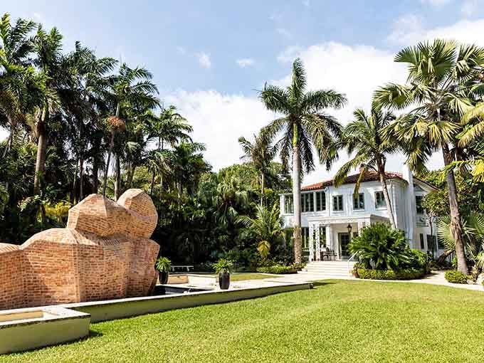 Brick sculptures rise from manicured lawns like ancient mysteries waiting beneath swaying palms and blue skies.