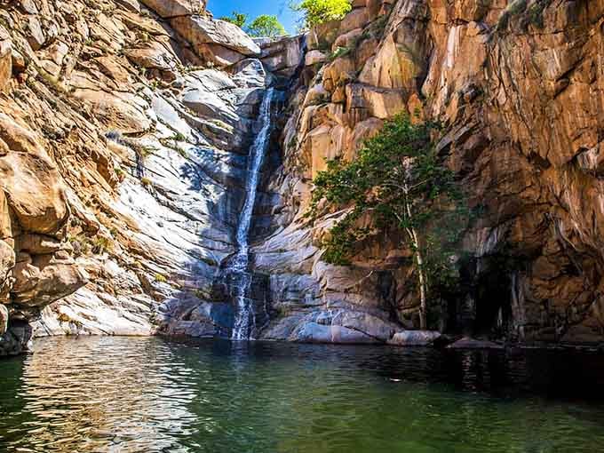 Towering canyon walls frame this ribbon of water as it plunges into a swimming hole that's pure desert oasis perfection.