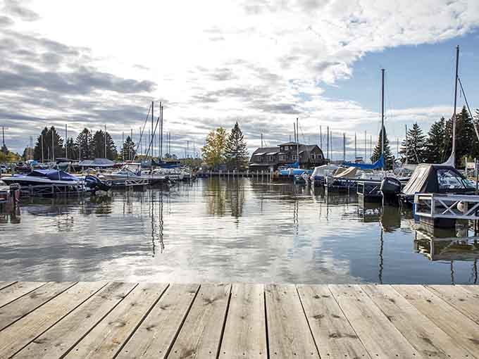 Boats bob gently in mirror-still water, their reflections doubling the peaceful beauty of this lakeside harbor scene.