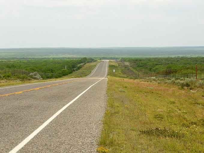 This arrow-straight highway disappears into the horizon where mountains float like purple dreams in the distance ahead.