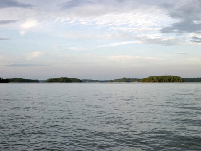 Forested islands dot the horizon under dramatic clouds, while gentle ripples catch the light across these pristine waters.