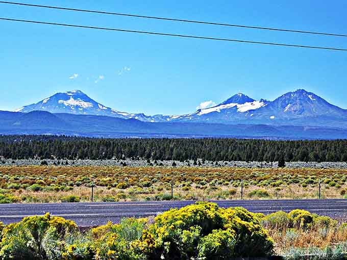Three volcanic sisters standing in a row, their snow-capped peaks rising above sagebrush like nature's own monument row.