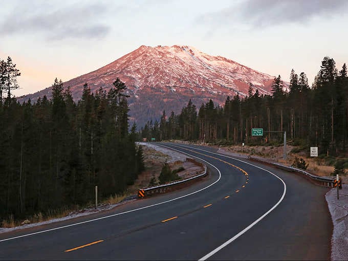 Golden sunrise bathes snow-dusted forests along curves that wind past alpine lakes like nature's own necklace of jewels.