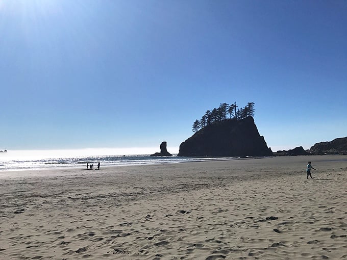 Golden sand stretches endlessly as silhouettes explore the tide line beneath towering rock formations.