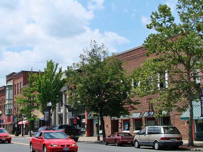 Brick storefronts and leafy trees frame streets where summer shopping feels like a pleasant journey through living history itself.