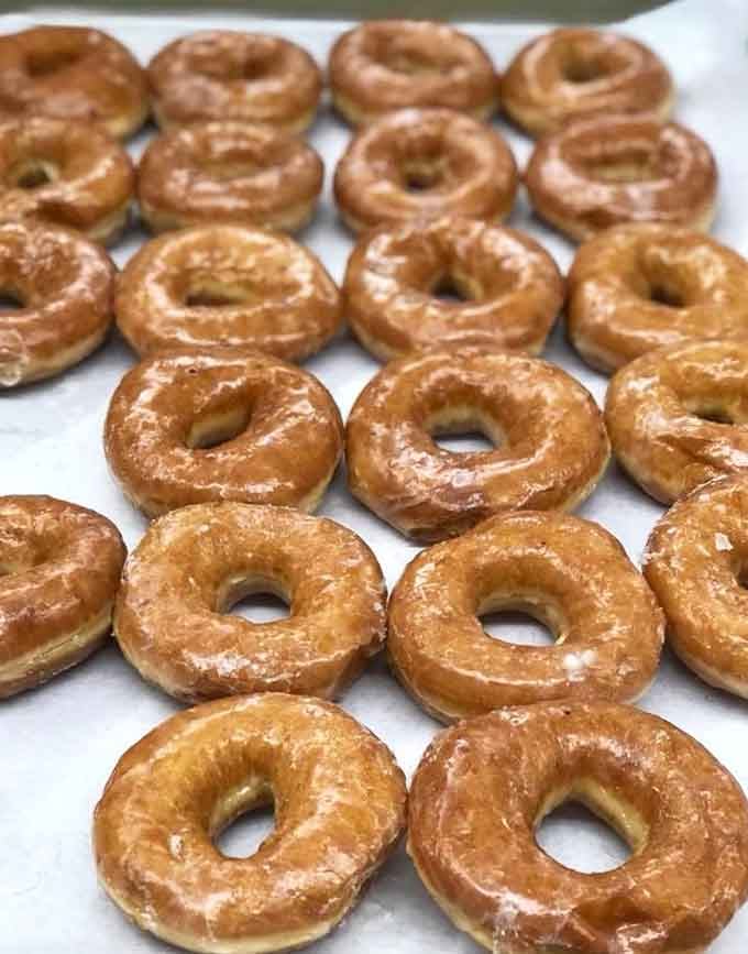Rows of glazed perfection catching the light like delicious halos, each one a small miracle of fried dough artistry.