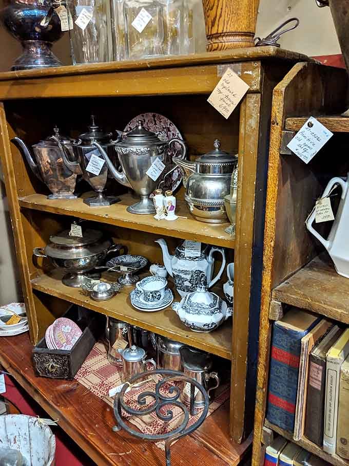 Silver tea sets gleam on wooden shelves, each piece ready to elevate your next gathering considerably.
