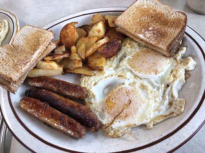 This plate delivers the holy trinity: perfectly cooked eggs, golden toast, and sausage links that justify getting out of bed early.