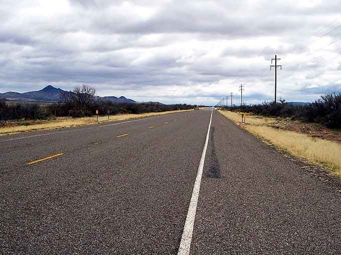 Power lines trace the route through wide open country where the road stretches endlessly toward distant blue mountains.