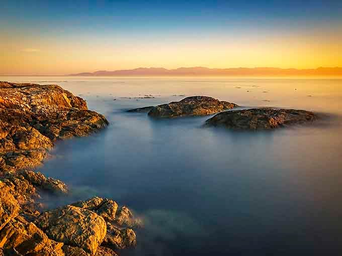 Golden hour transforms rocky shores into a dreamy watercolor where sea and sky blend into pure magic.