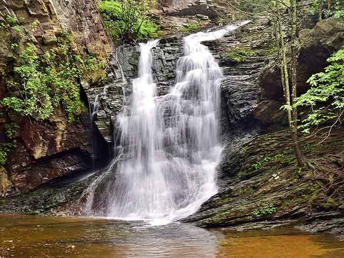 White water tumbles gracefully over layered rock formations into a swimming hole that's pure mountain magic.