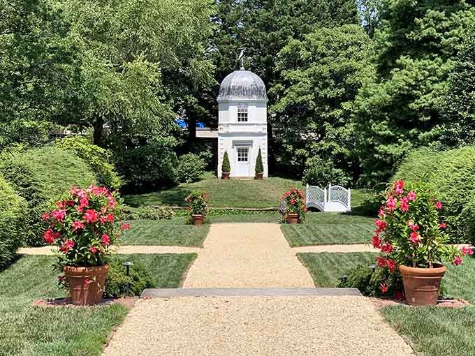 A white observatory tower stands at the end of a gravel path lined with potted roses in full bloom.