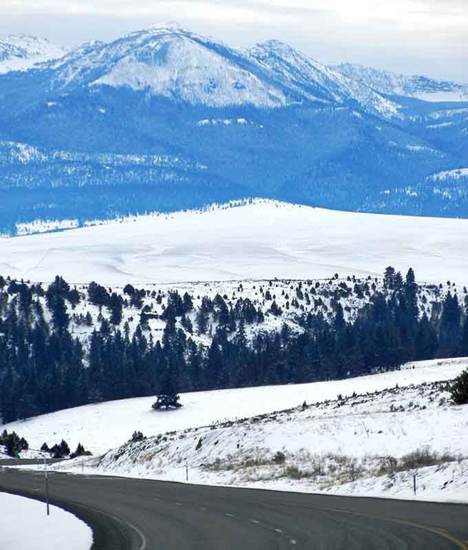 Winter transforms the landscape into layers of white and blue, where the road ribbons through like a photographer's dream.