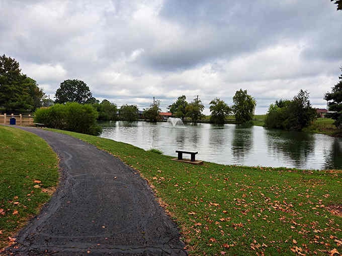 A peaceful walking path curves past still waters where a fountain dances, offering the perfect spot for quiet reflection.