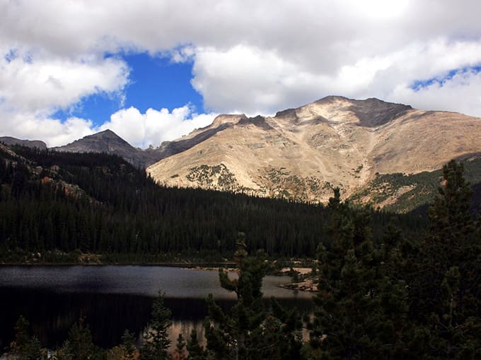 Dramatic mountain peaks tower over Sandbeach Lake's rare sandy shore, creating an unforgettable high-altitude beach experience worth the climb.