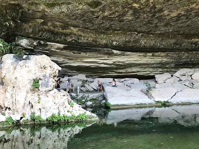 Families gather on ancient rock ledges beneath the grotto, sharing a swimming hole that predates human memory itself.
