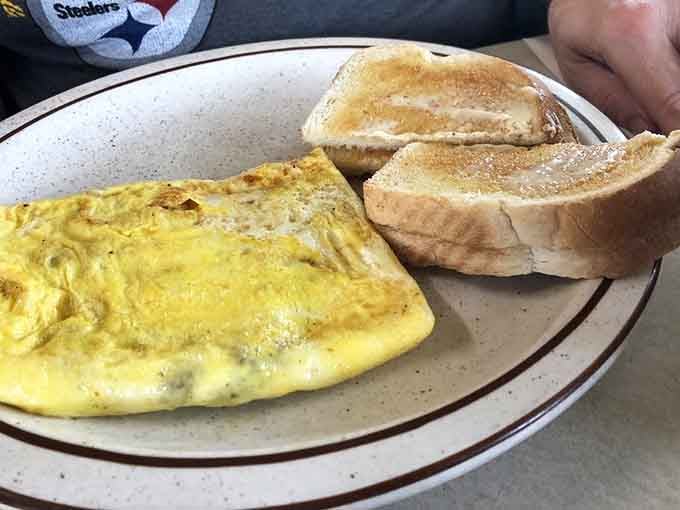 That fluffy omelet folded with care beside buttered toast represents everything right about simple food done exceptionally well every single time.
