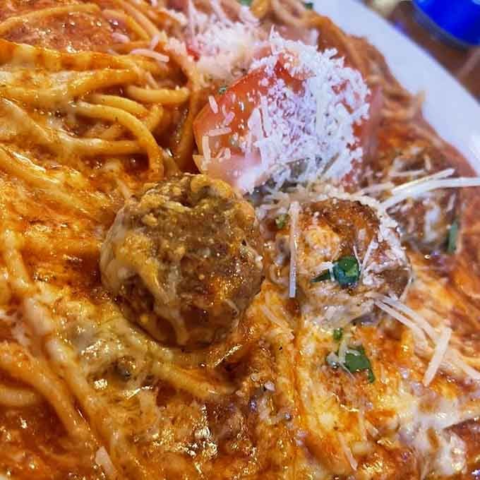 Meatballs nestled in spaghetti like they're exactly where they belong, covered in cheese because more is always more here.