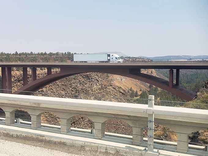 The modern highway bridge arches gracefully across the gorge while traffic zips by overhead, oblivious to glory.