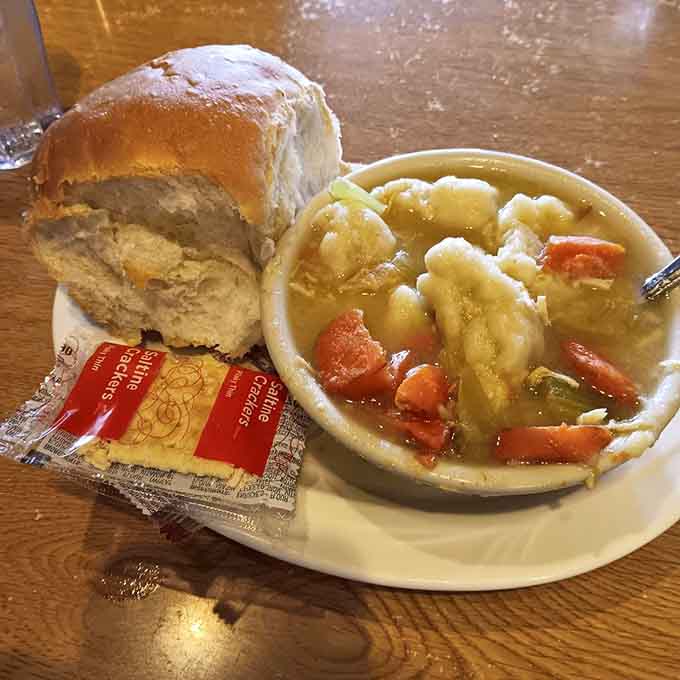 Homemade chicken dumpling soup beside a pillowy roll: a bowl that fixes whatever ails you.