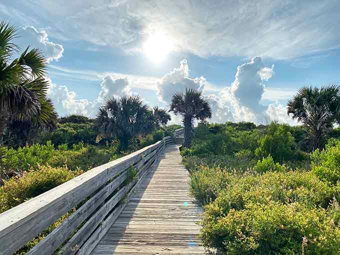 The boardwalk stretches through coastal dunes under dramatic clouds that paint the afternoon sky golden.