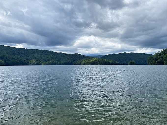 Dramatic storm clouds gather over mountain ridges while the lake's surface ripples with anticipation of approaching weather patterns.