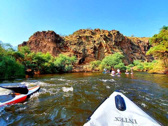 Desert cliffs frame this peaceful river bend where kayakers discover nature's own water park experience.