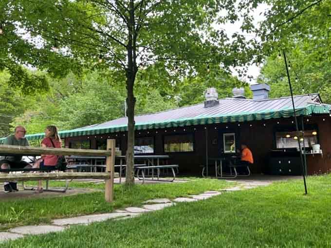 The green-striped awning and peaceful picnic tables create a park-like setting that makes every meal feel like a special occasion.