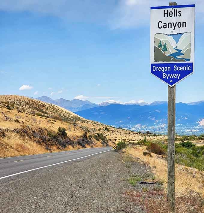 The Hells Canyon sign promises adventure ahead, standing proud against golden hills and distant blue mountain ranges beyond.